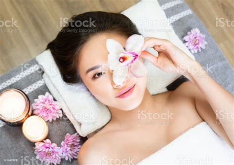 스파에서의 하루 스파 마사지 및 아로마 테라피 세션을 가진 아름다운 아시아 여성 예쁜 한국 젊은 여성이 난초 꽃을 얼굴에 들고