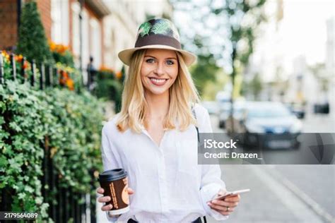밀짚 모자와 비즈니스 셔츠를 입고 스마트 폰을 사용하고 커피를 마시는 아름 다운 금발 중반 성인 여성 카메라를 보고 있는 사업가 25 29세에 대한 스톡 사진 및 기타