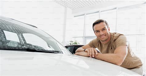 자동차 대리점에서 흰색 보닛에 기대어 행복을 보여주는 남자의 초상화 사진 Unsplash의 수송 이미지