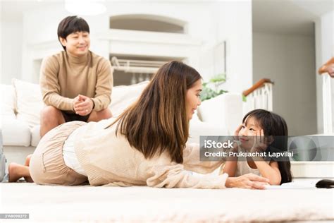 행복한 아시아 가족 바닥에 누워있는 작고 귀여운 딸과 아내를 보며 미소 짓는 아버지 등교 첫날 등교 준비를 위해 책을 읽고 있습니다 아이에 대한 선택적 집중 3 명에 대한