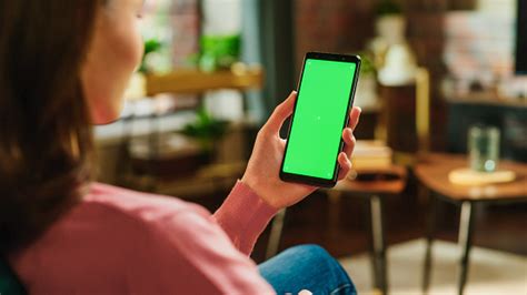 여성스러운 손으로 디스플레이를 탭하고 그린 스크린 모형 디스플레이가 있는 스마트폰의 피드를 스크롤합니다 여성은 집에서 쉬고