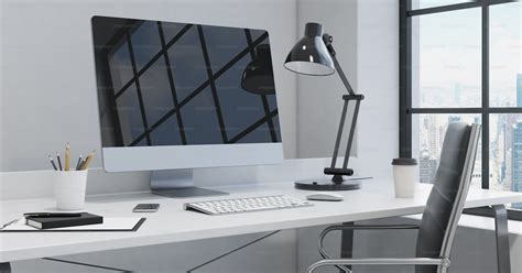 구석에 있는 직장 컴퓨터 키보드 마우스 스마트폰 램프 메모장 펜 연필 유리 테이블 위의 커피 앞 의자 오른쪽 창 도시 전망 일의 개념 사진