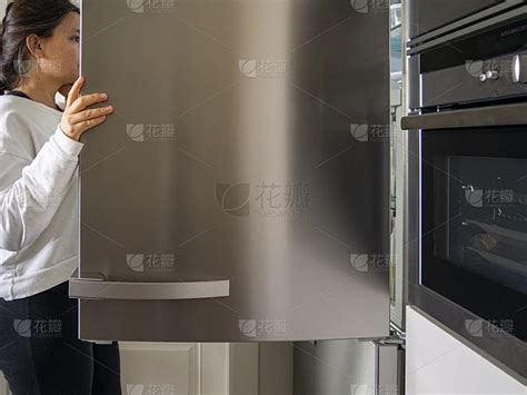 在家庭厨房里，一个女孩在打开的冰箱里寻找食物。素材 花瓣网