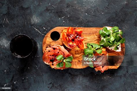 브루스 케 타 와인 세트 프로 슈 토 토마토 라이트 치즈 신선한 샐러드와 발사믹 크림이 있는 작은 샌드위치의 다양성은 어두운 배경 위에 소박한 나무 보드에 레드 와인과 함께