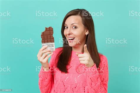 예쁜 젊은 여자에 파란색 벽 배경 스튜디오 초상화에 고립 된 손에 초콜릿 바 잡고 카메라에 분홍색 스웨터 포인팅 검지 니트 사람들의 라이프 스타일 개념입니다 복사 공간을