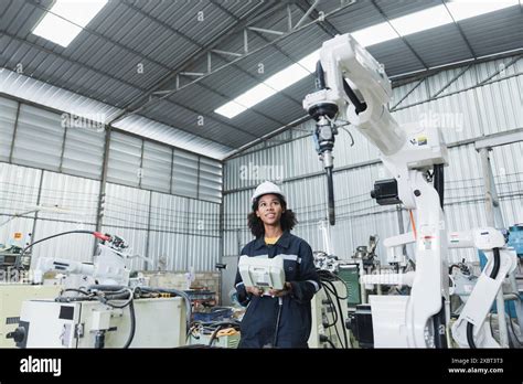 Engineer Controlling Robot Arm At Factory Checking The Operation Of