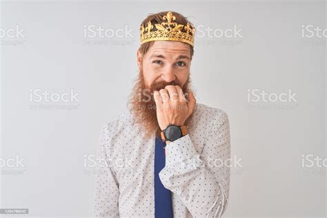 젊은 빨간 머리 아일랜드어 사업가 고립 된 흰색 배경 위에 왕관 왕을 입고 스트레스와 입을 물고 손톱에 손을 긴장 찾고 불안 문제 감정에 대한 스톡 사진 및 기타 이미지