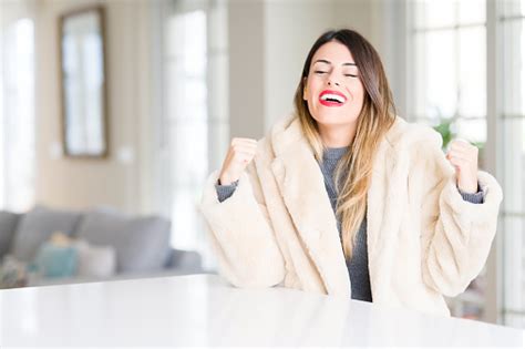 젊은 아름 다운 여자 집에서 매우 행복 하 고 흥분 무기와 우승자 제스처를 하 고 겨울 모피 코트를 입고 웃 고 성공을 위한 비명 축 하 개념입니다 갈색 머리에 대한 스톡