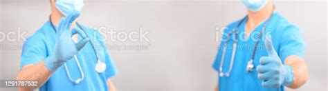 파란색 유니폼과 회색 배경에 의료 장갑을 끼고 있는 두 명의 의사 또는 의료진이 서로 마주치며 엄지손가락을 위로 또는 좋아하며 Ok를 보여줍니다 남자에 대한 스톡 사진 및