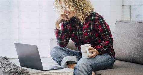 자유롭고 행복한 사람들의 개념은 사무실이 아닌 집에서 컴퓨터 기술로 일합니다 노트북을 가진 쾌활한 백인 여성은 배경에 창문이 있는 소파에 앉아 있습니다 사진