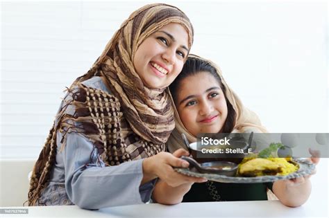 사랑스러운 웃는 파키스탄 무슬림 소녀와 부엌에서 어머니 전통 이슬람 음식의 쟁반을 잡고 딸과 엄마는 히잡을 착용하고 카메라에 할랄 음식을 보여주고 흰색 배경에 행복한 이슬람