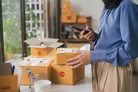 온라인 판매자는 모바일 앱을 사용하여 스마트 폰으로 배송 상자에 소포 바코드를 스캔합니다 25 29세에 대한 스톡 사진 및 기타 이미지 25 29세 Brand Name