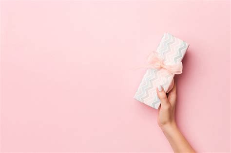 살아있는 산호 배경에 컬러 리본 줄무늬 선물 상자를 들고 여성의 손 크리스마스 컨셉 이나 다른 휴일 핸드메이드 선물 상자 카피 스페이스와 컨셉 탑 보기 강림절에 대한 스톡