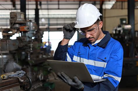 기술자 엔지니어 노동자 남자는 중공업 제조 공장에서 제어 또는 유지 보수 작업 선반 금속 기계를 제어하는 동안 서 있고 컴퓨터를 사용하는 보호 복을 진지하게 봅니다 25