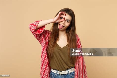 눈 근처에 손을 잡고 파스텔 베이 지 배경에 고립 안경 또는 쌍안경을 모방 혀를 보여주는 캐주얼 복장에 미친 젊은 여자 사람들의 감정 라이프 스타일 개념입니다 복사 공간을