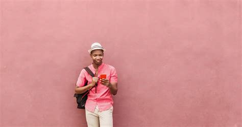 배낭과 모자를 쓴 라틴 아메리카 남자가 스마트폰 모바일을 바라보는 화려한 벽 위에 서 있다 사진 Unsplash의 브랜드 이름 스마트 폰 이미지