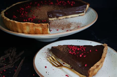 골드 포크 바삭바삭하고 플루티드 페이스트리 크러스트가 달린 화이트 브라운 테두리 접시에 담긴 초콜릿 타르트 슬라이스의 클로즈업 이미지 코코아 파우더로 뿌려진 코코아 파우더