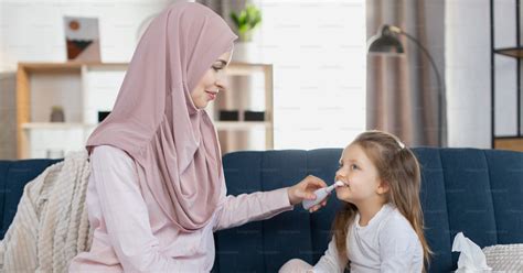 행복한 아랍 가족 아침 위생 히잡을 쓴 무슬림 어머니 집 소파에 앉아 전동 칫솔로 귀여운 딸 아이의 양치질 치아 추진 청소 방법 보여주기 사진 Unsplash의