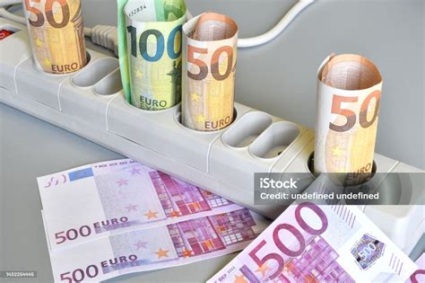 유로 지폐는 굴러 올라 회색 배경의 전기 확장 소켓의 전기 소켓에 삽입되었습니다 전기 비용 상승에 대한 개념 비싼 에너지 요금과 전기 가격 상승 0명에 대한 스톡 사진 및