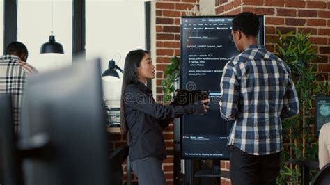 Team Of Coders Analyzing Code On Wall Screen Tv Comparing Errors Using Digital Tablet Stock