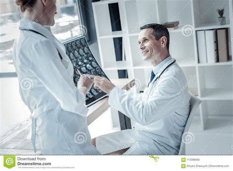 Pleasant Skilled Doctor Sitting And Looking At His Colleague Stock