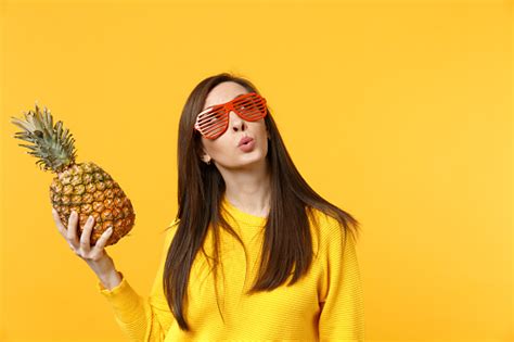 스튜디오에서 노란색 오렌지 배경에 고립 된 신선한 잘 익은 파인애플 과일을 들고 찾고 재미 안경에 잠겨있는 젊은 여자 사람들은 생생한 라이프 스타일 휴식 휴가 개념입니다
