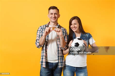 젊은 커플 여자 남자 팬 들고 Bitcoin 금속 황금 동전 축구공 노란색 배경에 고립 된 지원 팀을 응원 하는 축구 승리 스포츠 베팅 흥분 열정 가족 라이프 스타일