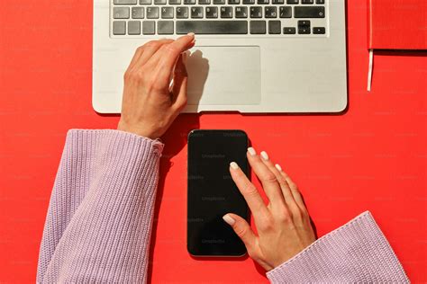 빨간 책상 위에서 전화기와 노트북을 손이 사용하고 있습니다 사진 Unsplash의 기술 이미지