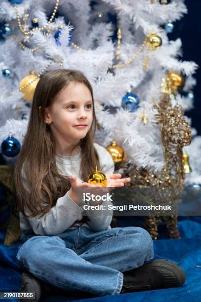 안경을 쓴 작고 귀여운 소녀가 매력과 화환으로 크리스마스 트리 앞에 앉아 있습니다 재미 있는 어린이 파티의 개념 6 7 살에 대한 스톡 사진 및 기타 이미지 Istock