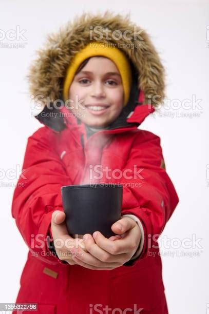 เด็กชายวัยเรียนที่ร่าเริงน่ารักในเสื้อผ้าที่อบอุ่นสดใสยิ้มฟันมองไปที่กล้องอุ่นมือของเ ภาพสต็อก