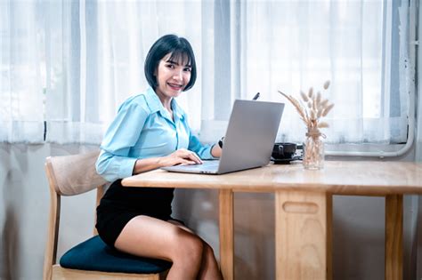 아시아 프리랜서들의 치과 교정기로 미소를 짓고 있는 여성 캐주얼은 커피숍의 카페 인테리어에서 커피컵과 스마트폰이 있는 노트북 컴퓨터와 노트북으로 일하고 있다 25 29세에