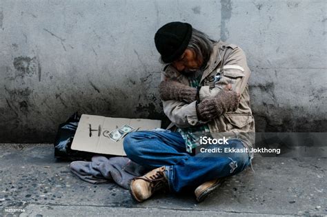 길가에 살 집도 없고 일도 없기 때문에 지나가는 사람들에게 도움을 청하는 표지판을 들고 보도에 앉아있는 노숙자 노인의 초상화 굶주림과 함께 60 64세에 대한 스톡 사진 및
