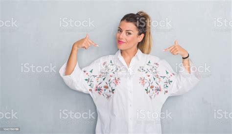 그런 지 회색 벽 입고 위에 젊은 성인 여자 꽃 셔츠 보고 얼굴에 미소와 자신감 자랑 스럽게 생각 하 고 행복 한 손가락으로 자신을 가리키는 가리키기에 대한 스톡 사진 및