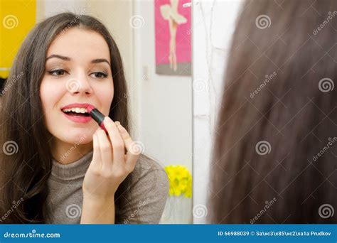 Beautiful Girl Putting Lipstick In Front Of The Mirror Stock Image