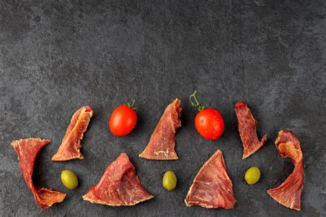 유기농 수제 식품 어두운 배경에 매운 육포 고기조각 조미료와 거친 소금 붉은 체리 토마토 올리브 맥주 에 대한 천연 간식 맨 위 보기입니다 플랫 레이 공간을 복사합니다 0