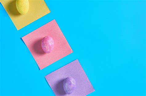 반짝이와 사각형 종이 스티커와 세 개의 다채로운 계란의 행은 부엌에 파란색 책상에 놓여있다 부활절 개념입니다 텍스트의 공백입니다 맨 위 보기 3가지 개체에 대한 스톡 사진