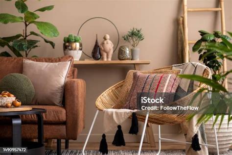 갈색 소파 꼰 안락의자 무늬 베개 둥근 커피 테이블 세련된 조각품 화분 식물 및 개인 액세서리가 있는 거실 인테리어의 인테리어 디자인 가정 장식 템플렛 0명에 대한 스톡