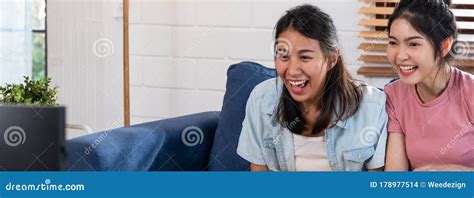 Happy Asian Lesbian Couple Watching Television Together At Sofa In