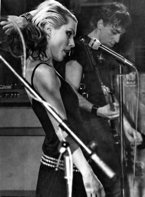 A Woman Standing In Front Of A Microphone While Another Man Stands Behind Her And Sings