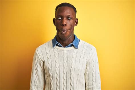 고립 된 노란색 배경 위에 데님 셔츠와 흰색 스웨터를 입은 아프리카 계 미국인 남성이 입술 미친 코믹 한 제스처로 물고기 얼굴을 만듭니다 재미있는 표현 겨울에 대한 스톡