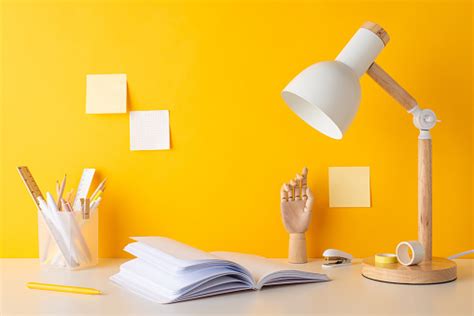 학업 준비 설정 연필 펜 자 접착 테이프 열린 알림 마네킹 손 스테이플러 램프 및 스티커 메모가 노란색 벽에 책상 위에 깔끔하게 배열되어 있는 측면 사진 0명에 대한 스톡