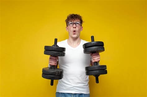 Premium Photo Young Surprised Nerd Guy In Glasses Holds Heavy Dumbbells And Angrily Shouts On