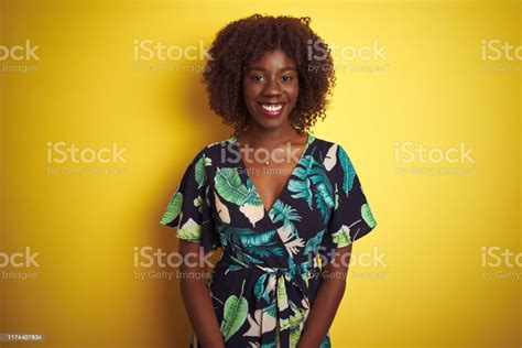 고립 된 노란색 배경 위에 여름 꽃 드레스를 입은 젊은 아프리카 아프로 여성얼굴에 행복하고 시원한 미소 운이 좋은 사람 곱슬