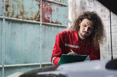 후드가 열린 차량 엔진 구역 옆에 체크리스트가 있는 젊은 백인 자동차 정비사 차고에서 현대 자동차를 확인하는 기술자 자동차 수리