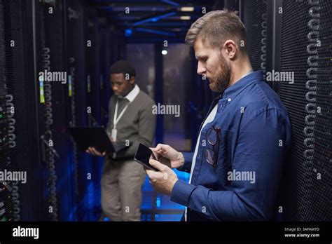 Engineers Working In A Modern Data Center Server Room Checking Devices And Maintaining Server