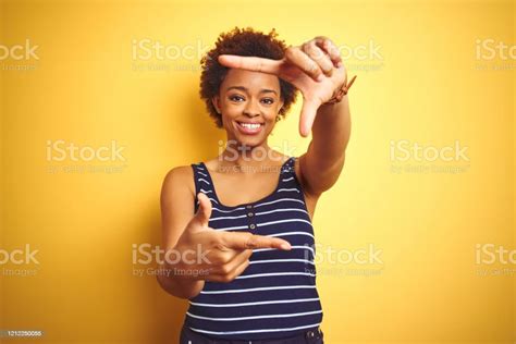 아름다운 아프리카 계 미국인 여성은 행복한 얼굴로 손과 손가락으로 프레임을 만드는 고립 된 노란색 배경 위에 여름 티셔츠를 입고 있습니다 창의력과 사진 개념 T 셔츠에 대한