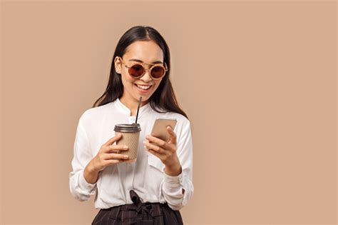 자유형 셔츠와 선글라스에 젊은 여자 서 고립 된 가방 과 컵 의 커피 브라우징 스마트 폰 행복 갈색 머리에 대한 스톡 사진 및