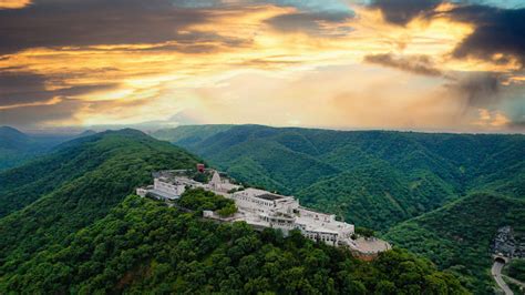가트 키 구니 터널 이후 아그라 자이푸르 로드에 있는 유명한 랜드마크 출기리 자이나교 사원 무성한 녹색 아라발리 언덕 산 꼭대기에 자리 잡은 흰색 건물을 보여주는 공중 드론