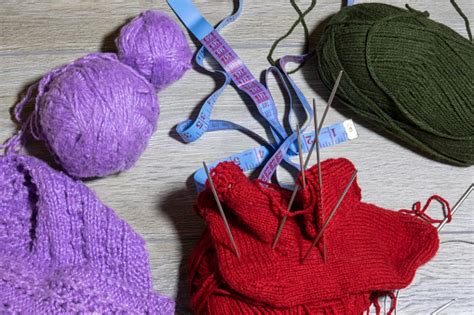 빨간 양말과 라일락 스웨터는 회색 나무 테이블에 바늘로 뜨개질하는 과정에서 회색 나무 테이블에 빨간색 라일락 및 짙은 녹색의 실을 꽂습니다 0명에 대한 스톡 사진 및 기타