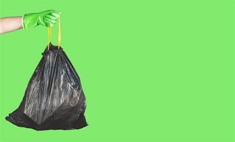 쓰레기로 가득 찬 검은색 플라스틱 일회용 쓰레기 봉투의 손잡이를 잡고 장갑을 끼고 텍스트에 대한 복사 공간이 있는 녹색 배너 배경에 낭비 쓰레기 봉투에 대한 스톡 사진 및